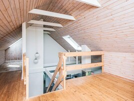 Quarto de sótão amplo, com pé direito alto, vigas de madeira, claraboia e escada de madeira.