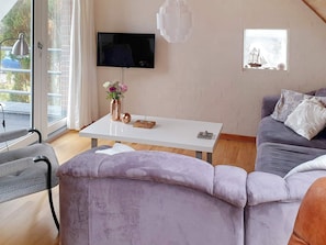 Uma sala de estar moderna com um sofá, uma mesa de centro branca, uma TV de tela plana e uma pequena janela com decoração náutica.