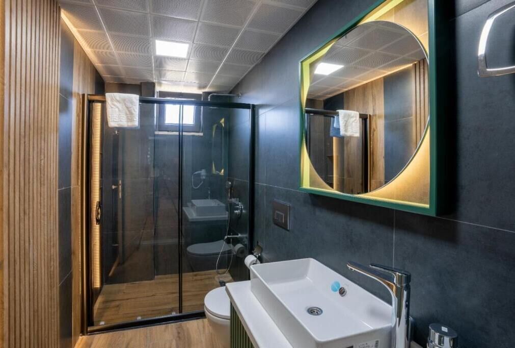 Uma casa de banho moderna com cabine de duche em vidro, lavatório branco e espelho com moldura verde.