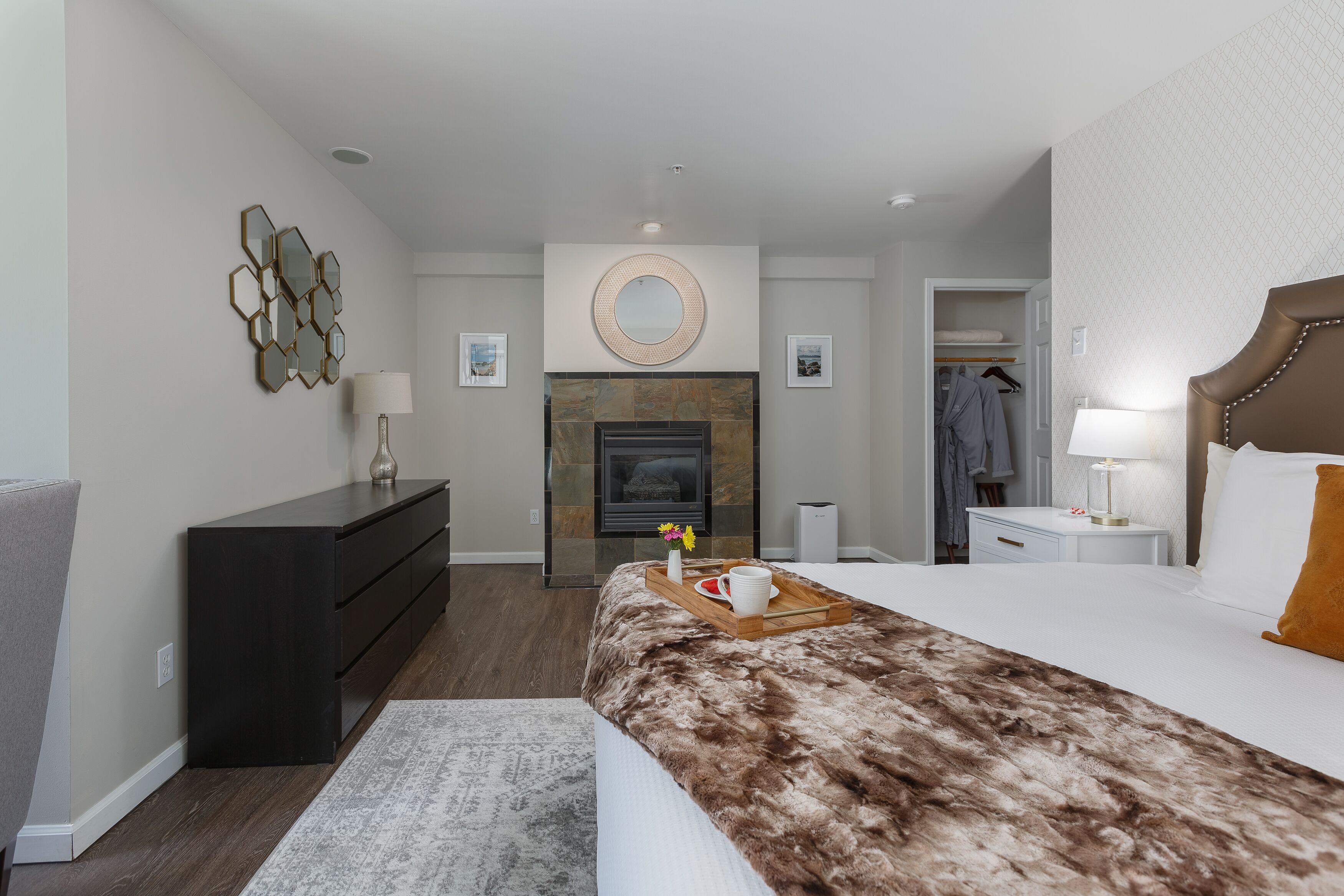 Quarto moderno com uma cama grande, cômoda, espelho e lareira.