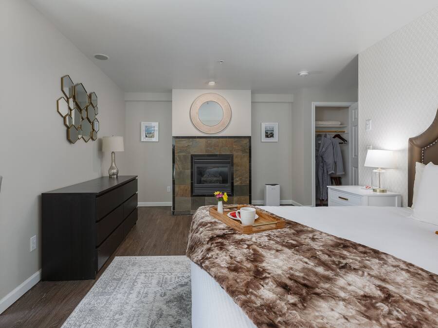 Quarto moderno com uma cama grande, cômoda, espelho e lareira.