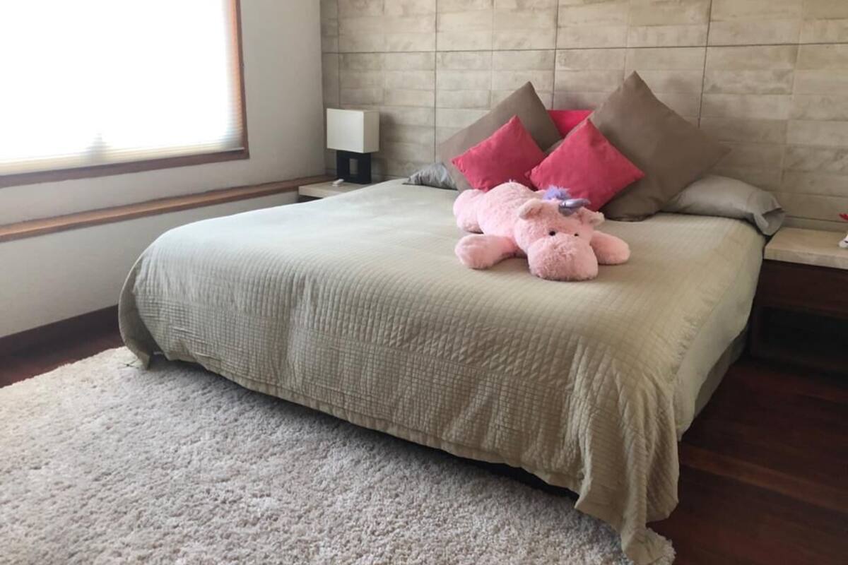 Cama bem arrumada com colcha verde, duas almofadas e um brinquedo de pelúcia rosa.