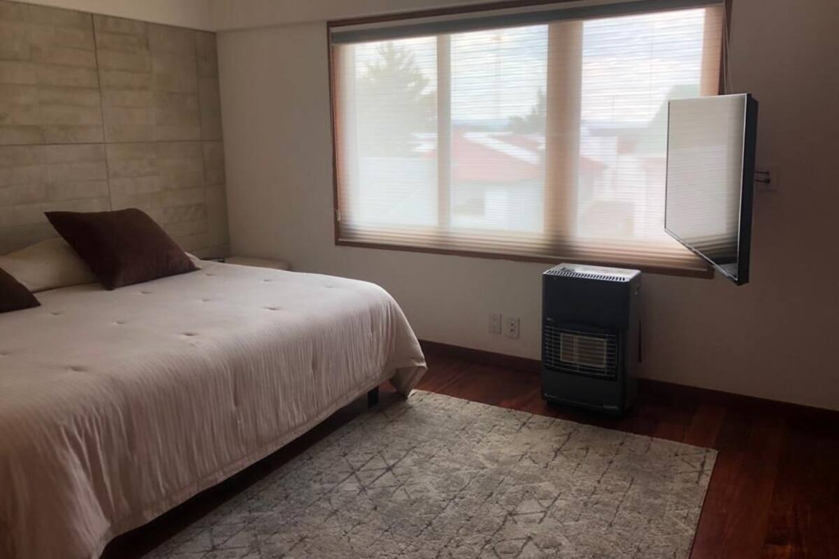 Quarto com cama, janela, aquecedor e televisão presa na parede.