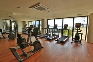 Uma academia com esteiras, elípticos e bicicletas ergométricas, grandes janelas com vista para o exterior.