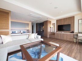Quarto de hotel moderno com sofá, mesa de centro de vidro, televisão e cozinha.