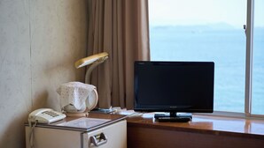 Quarto de hotel com escrivaninha, monitor de computador, telefone e luminária.