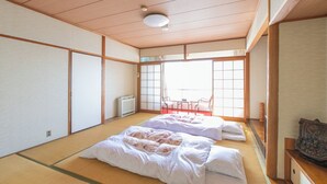 Um quarto japonês tradicional com tatames, duas camas, uma porta deslizante e vista para o exterior.
