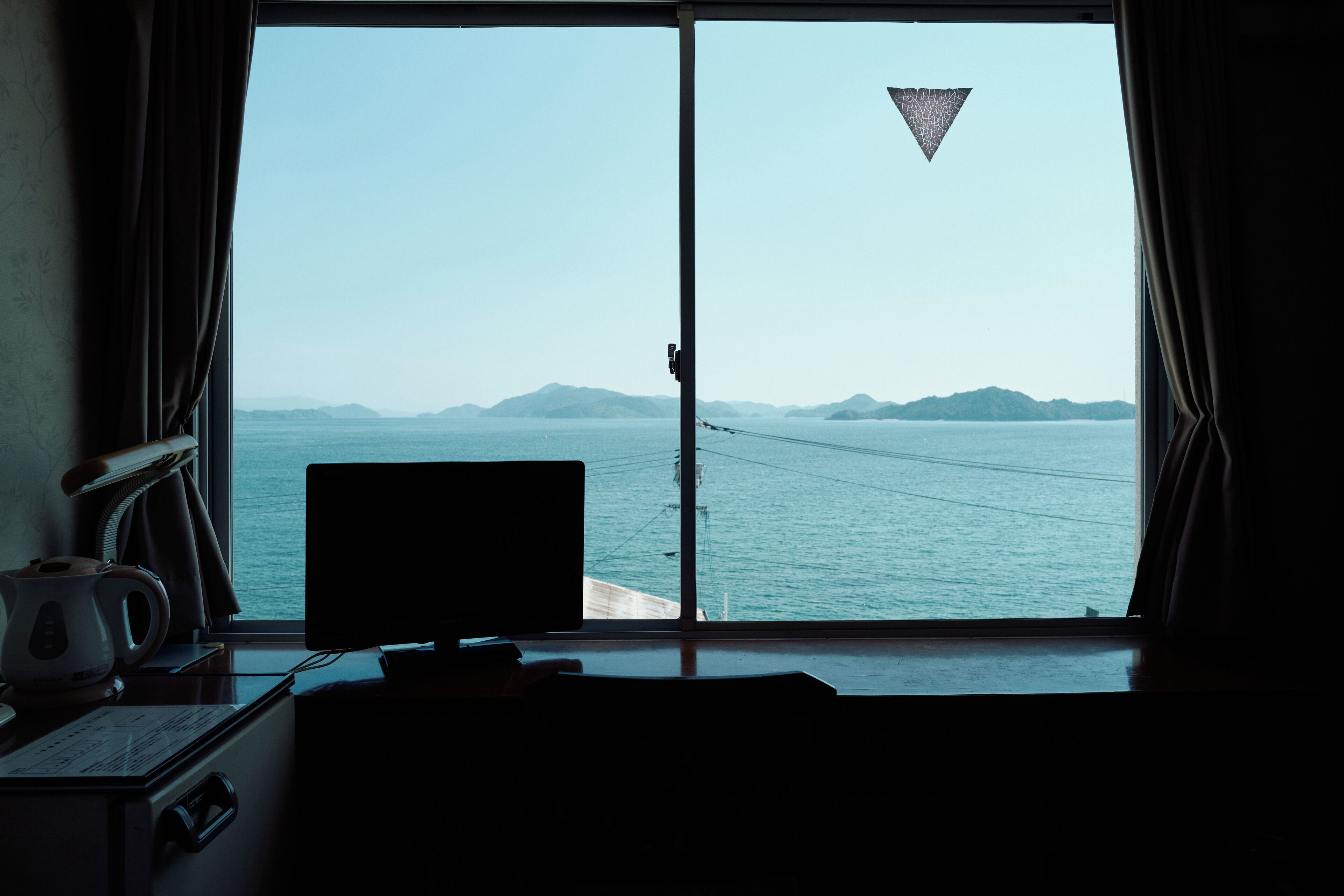 Quarto com escrivaninha, laptop e vista para o mar e montanhas.