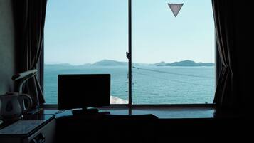 Quarto com escrivaninha, laptop e vista para o mar e montanhas.