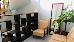 Uma sala de estar com um sofá bege, uma cadeira, uma estante preta e um espelho.