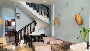 Uma sala de estar moderna com uma escada curva, uma área de jantar e uma cozinha ao fundo.