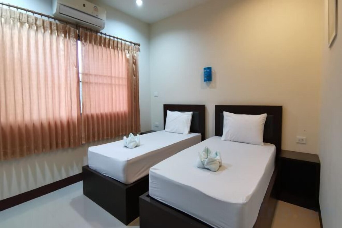 Quarto de hotel com duas camas de solteiro, janela com cortinas, ar condicionado e uma mesinha de cabeceira.