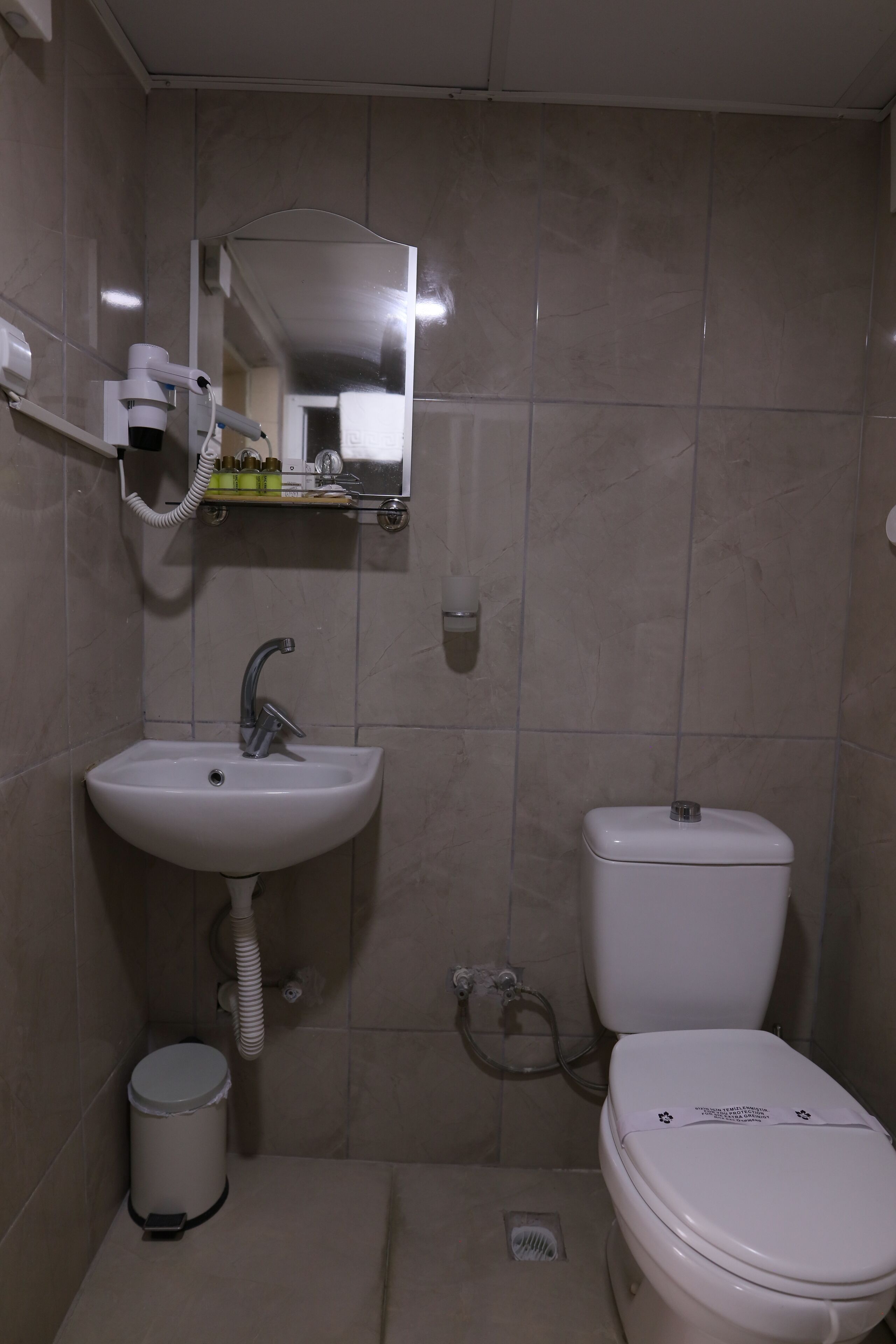 Um banheiro com pia branca, espelho, vaso sanitário e lixeira.