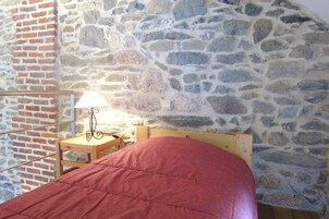 Quarto com parede de pedra, cama de madeira, mesa de cabeceira com abajur e parede de tijolos.