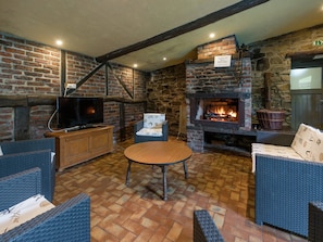 Um quarto aconchegante com lareira de pedra, televisão, móveis de vime e piso de azulejos.