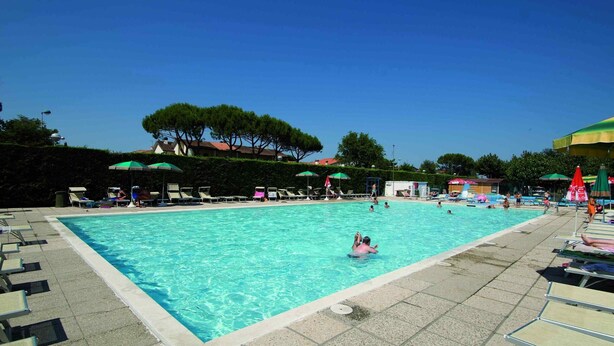 Piscina com espreguiçadeiras e guarda-sóis, rodeada por árvores e edifícios.