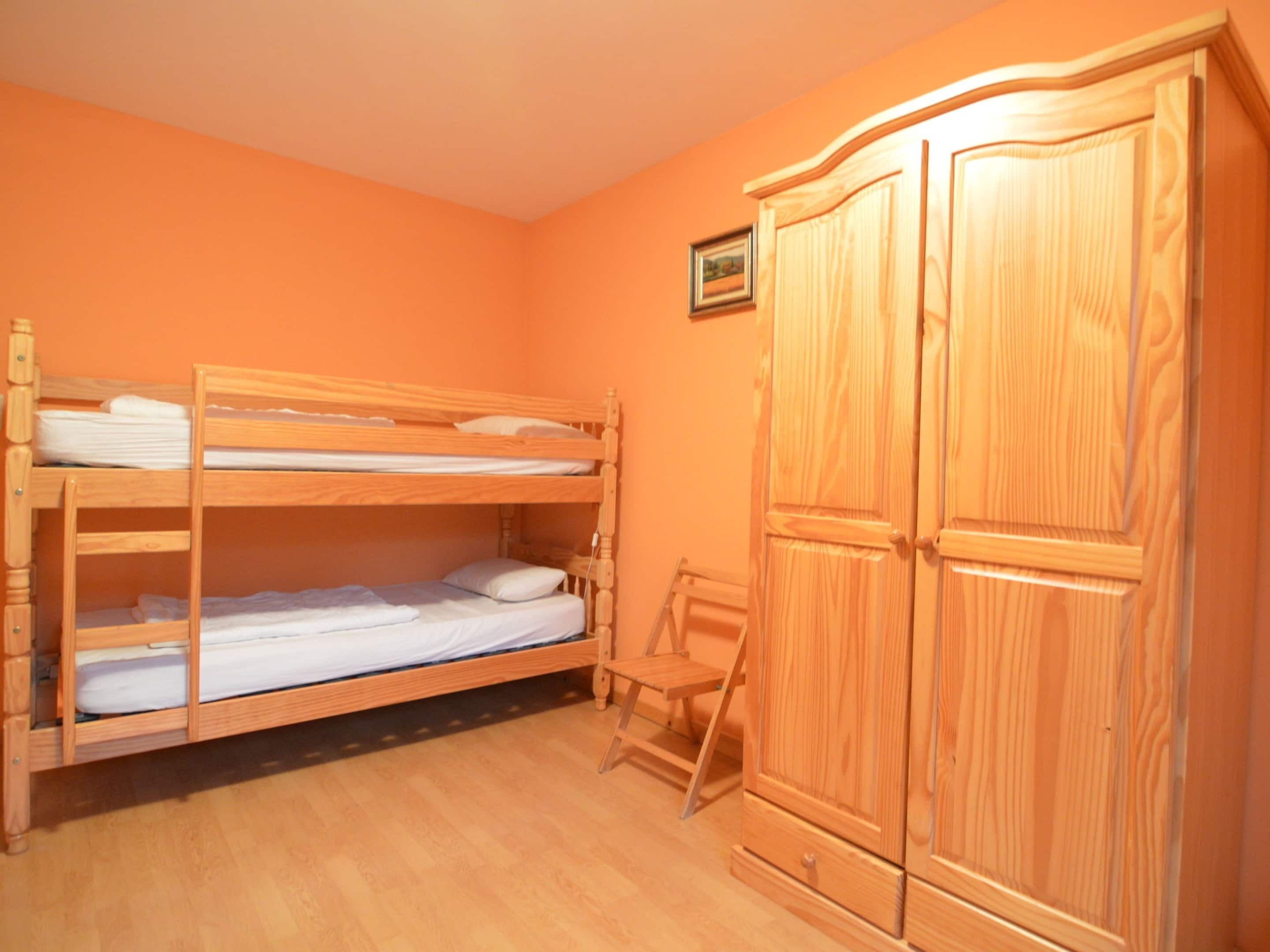 Quarto com duas beliches, um guarda-roupa de madeira e uma cadeira de madeira.