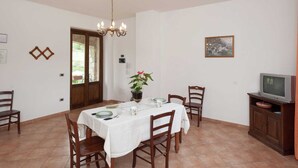 Uma sala de jantar com uma mesa posta para quatro pessoas, rodeada por cadeiras, um lustre e uma televisão em um móvel.