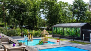 Piscina com escorrega e área de recreação, rodeada por espreguiçadeiras de madeira e uma área cercada.