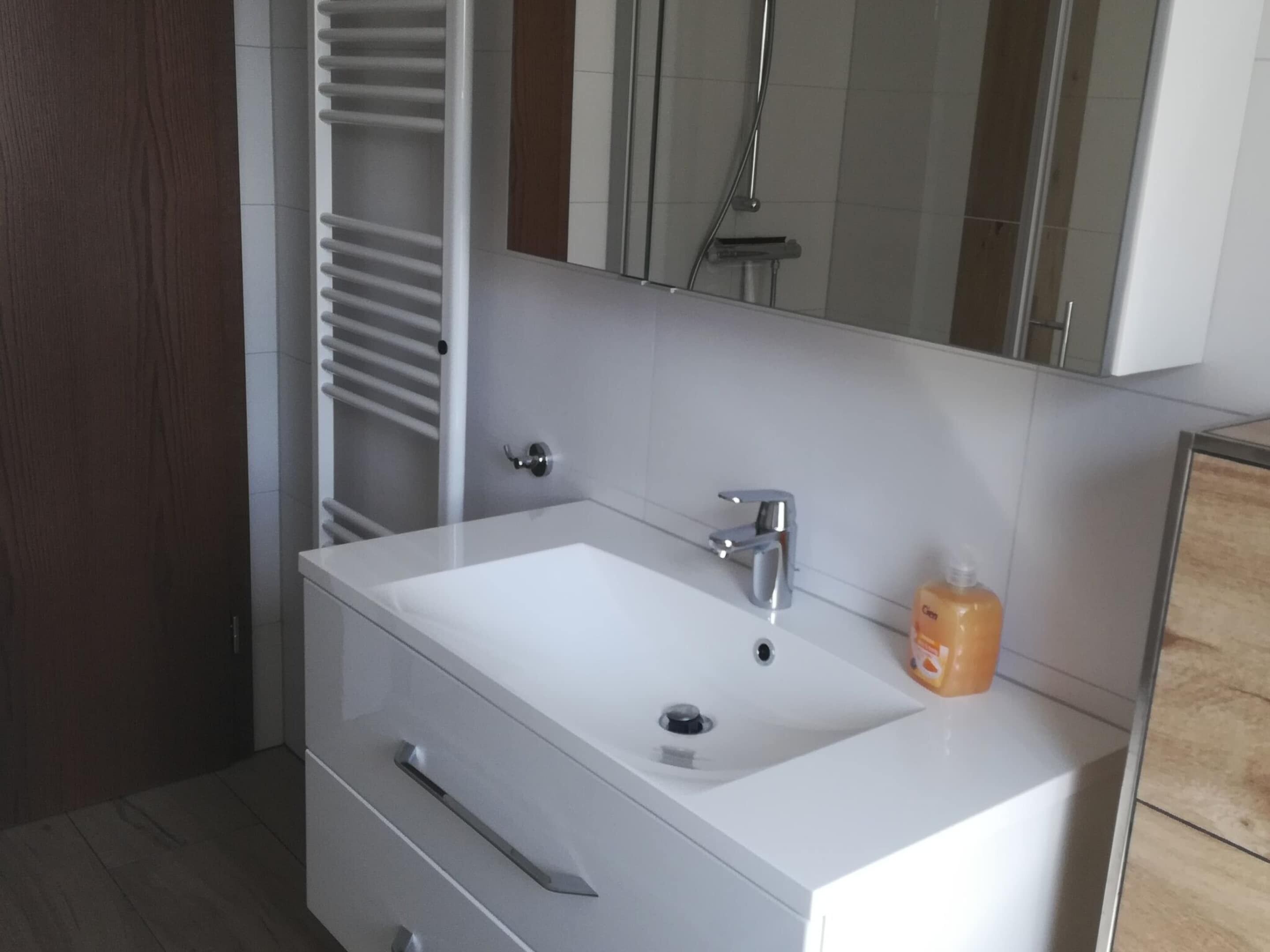 Uma casa de banho moderna com uma pia branca, um espelho e um porta-toalhas.