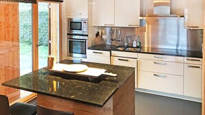 Cozinha moderna com armários brancos, bancada de granito e eletrodomésticos de aço inoxidável, incluindo micro-ondas, forno e geladeira.