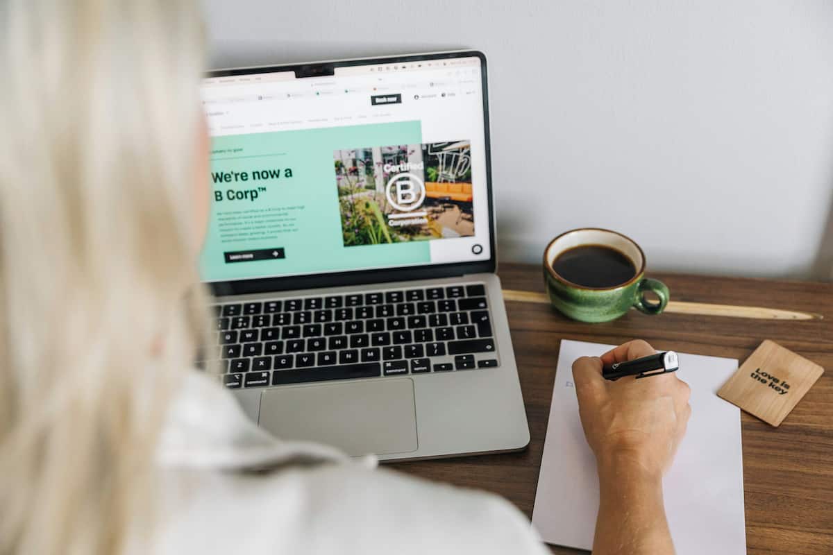 Um laptop sobre uma mesa, com uma caneca verde, uma caneta e um apoio para copo com a inscrição 'Love is the key'.