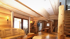 Interior de uma cabana de tronco com sofá, banqueta, mesa de centro de madeira e um espaço de jantar com bancos.