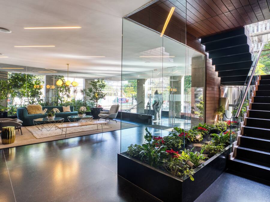 Um interior moderno com separação em vidro, escada e área de estar com plantas.