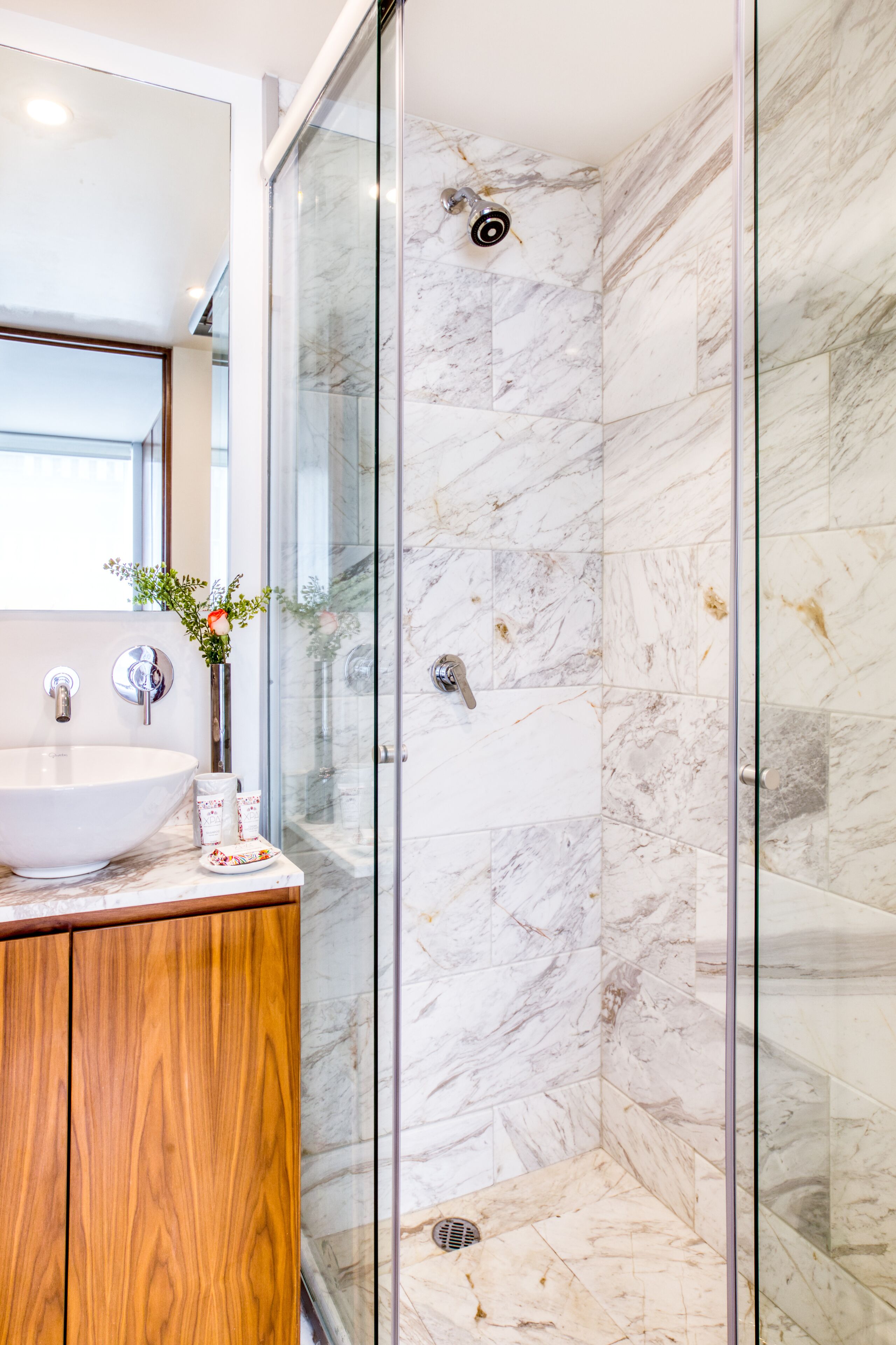 Um banheiro moderno com chuveiro de vidro, azulejos de mármore e toucador de madeira.