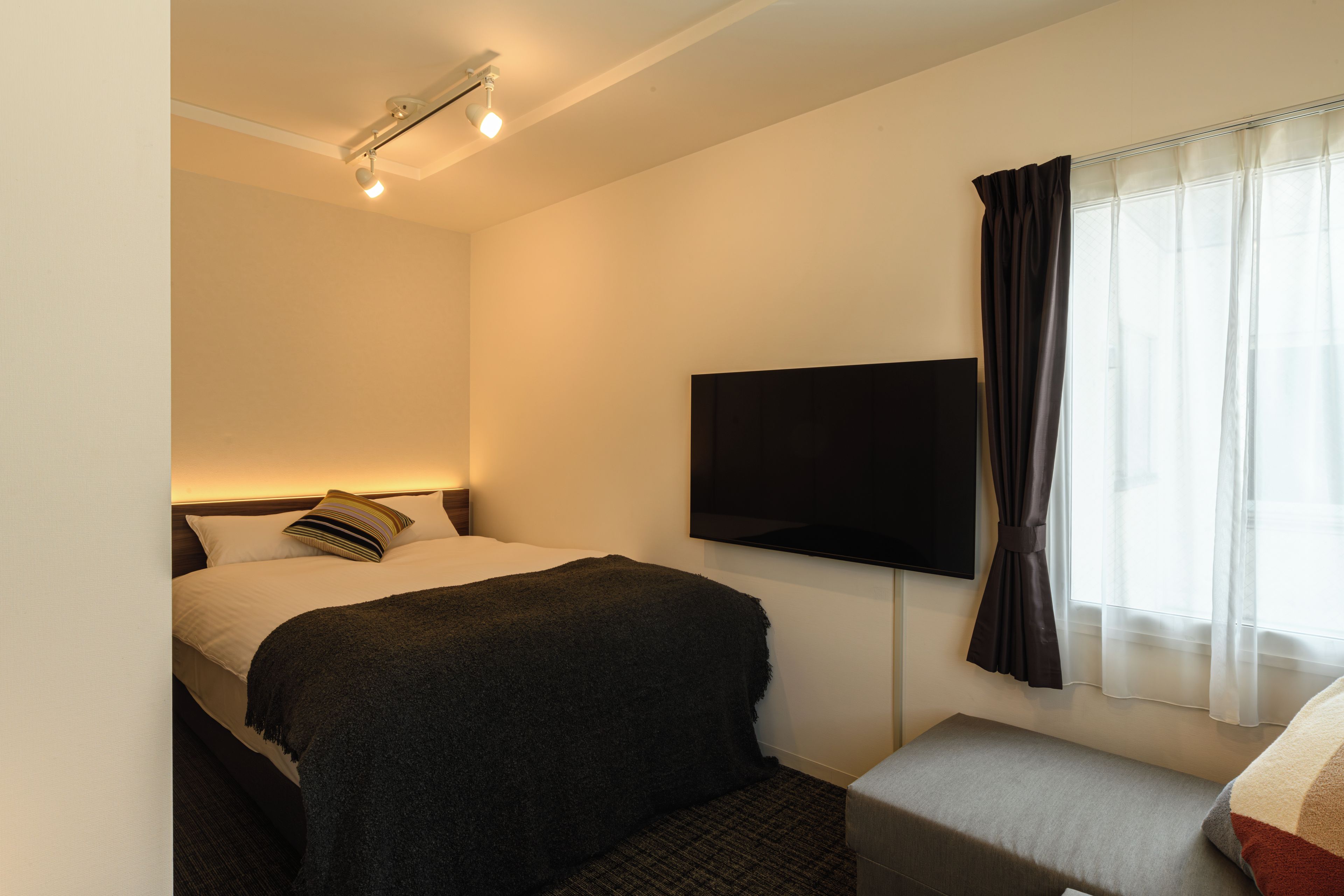 Quarto de hotel com cama, TV de tela plana na parede, janela com cortinas e um pequeno espaço para sentar.