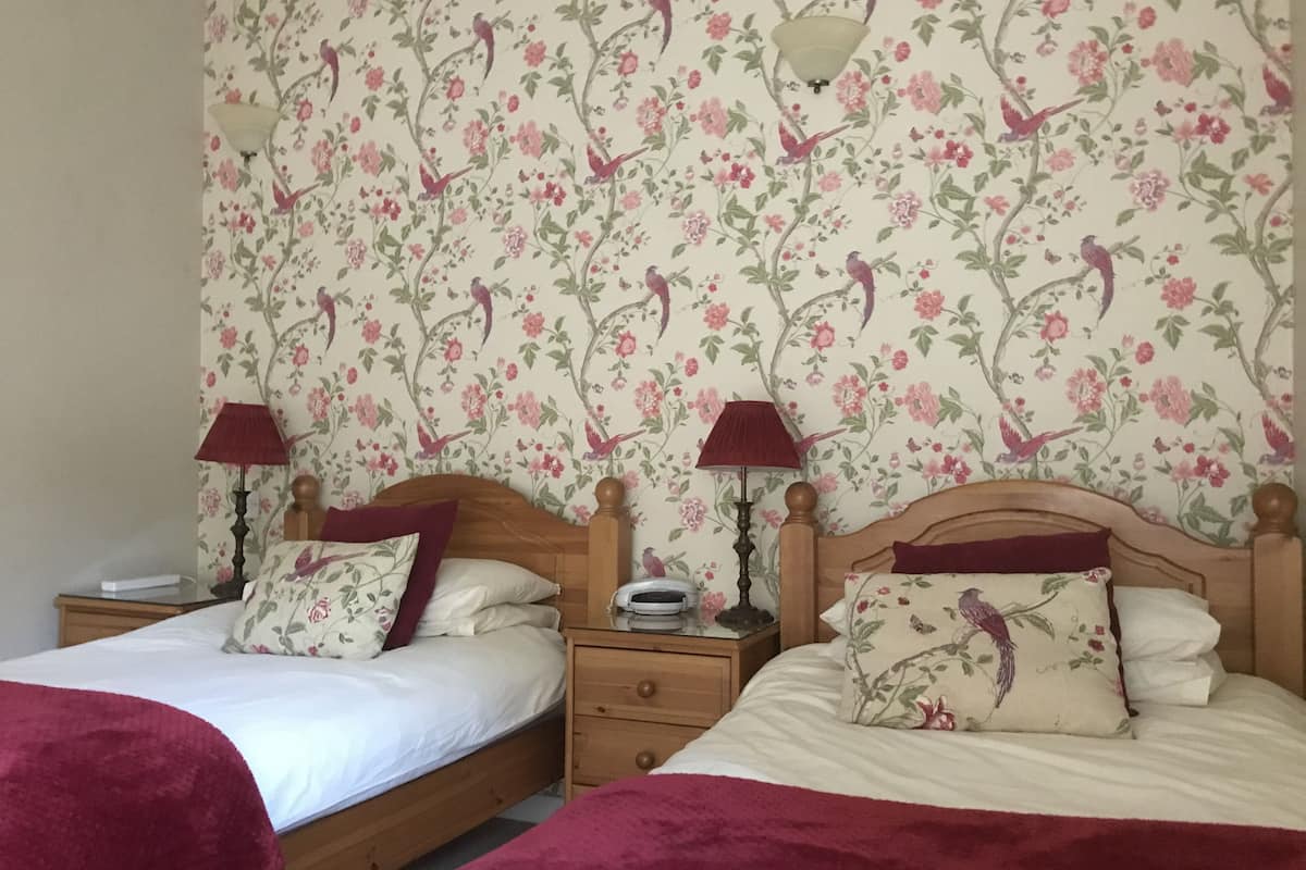 Quarto com duas camas de madeira, cada uma com luminária vermelha e roupa de cama estampada com motivos florais.
