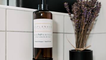 Um frasco de loção Esplanade para mãos e corpo sobre uma bancada branca, ao lado de um vaso preto com lavanda.
