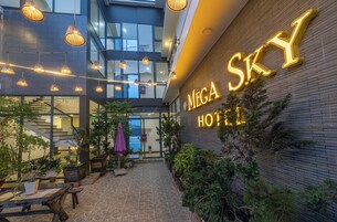 Entrada de um hotel com uma placa indicando "MEGA SKY HOTEL" e área de estar externa com vasos de plantas.