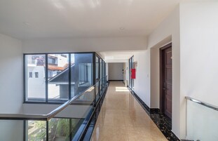 Um corredor com guarda-corpos de vidro, piso de mármore e vista para edifícios.