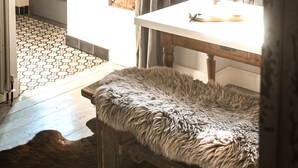 Quarto com parede de pedra, um banco, uma mesa e uma janela com cortinas.
