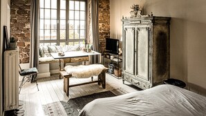 Quarto aconchegante com parede de pedra, um banco de madeira, uma mesa com abajur, uma televisão em uma prateleira e uma cama.