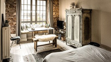 Quarto aconchegante com parede de pedra, um banco de madeira, uma mesa com abajur, uma televisão em uma prateleira e uma cama.