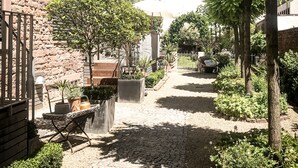 Uma passagem de calçada flanqueada por vegetação e um edifício de pedra com um grande guarda-sol.