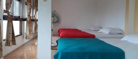 Quarto com duas camas, um ventilador e cortinas.