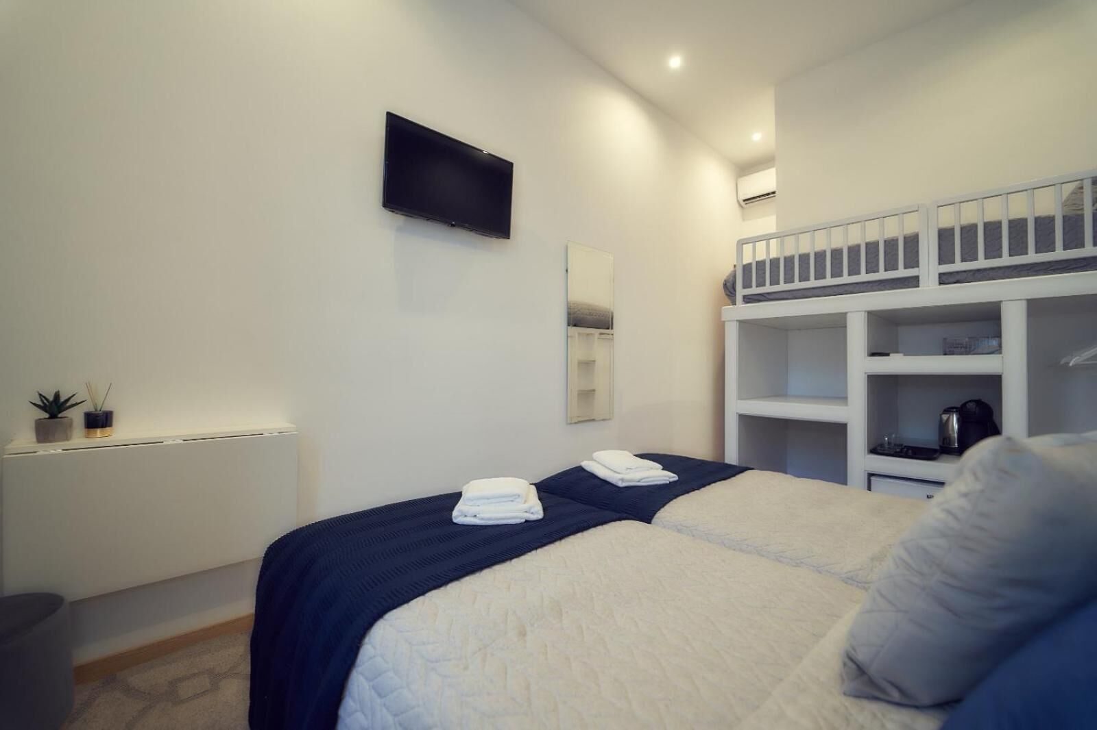 Quarto de hotel moderno com cama, televisão na parede, armário embutido e uma pequena planta no criado-mudo.