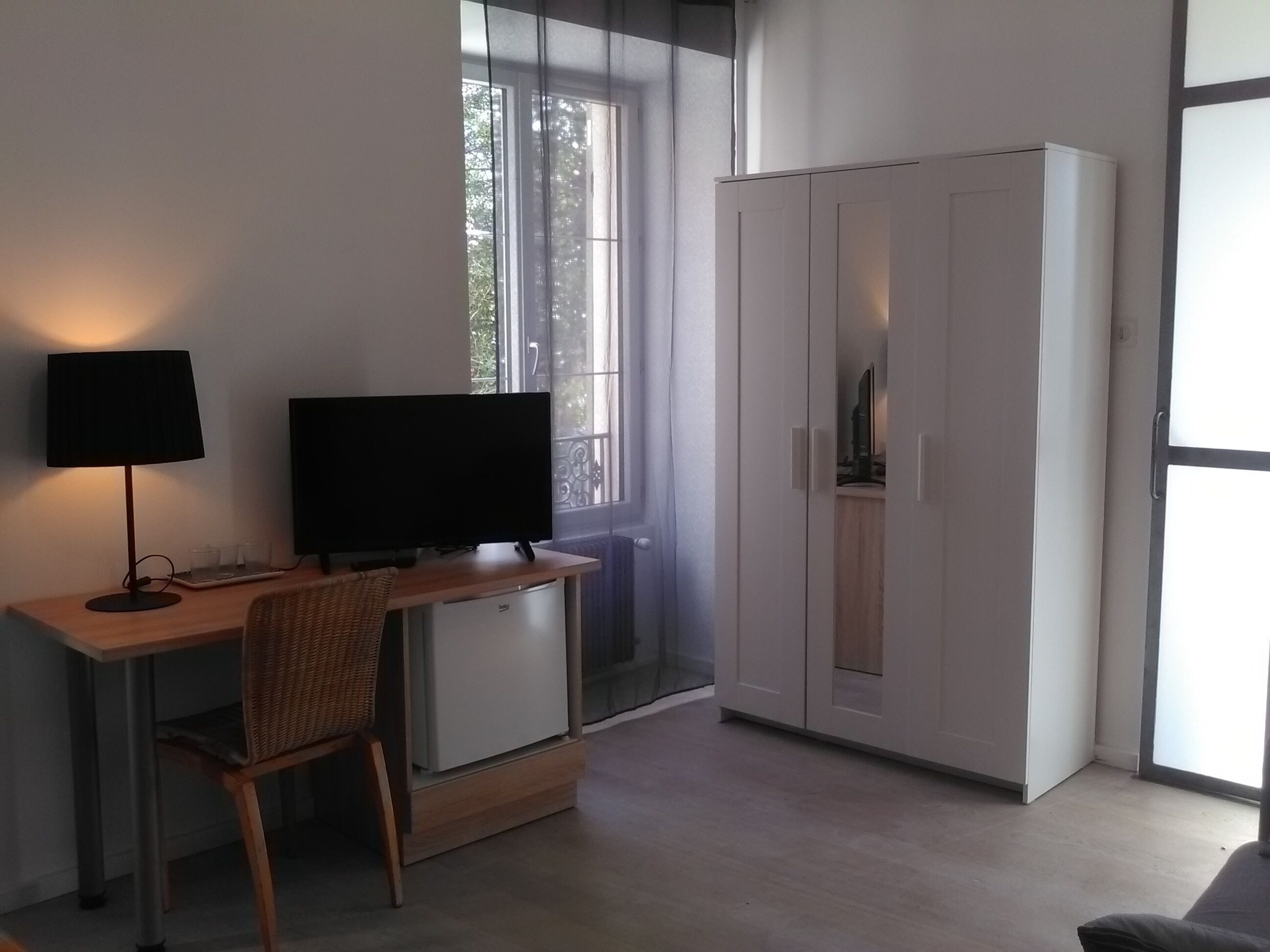 Quarto moderno com escrivaninha, cadeira, televisão, guarda-roupa e um pequeno frigorífico.