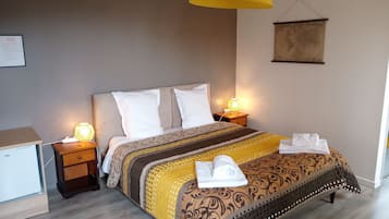 Cama bem arrumada com colcha estampada e almofadas, duas luminárias de cabeceira, uma pequena mesa de cabeceira de madeira e um mapa fixado na parede.