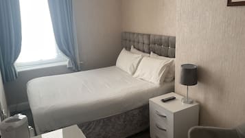Quarto de hotel bem arrumado, com cama, mesa de cabeceira, luminária e janela com cortinas.