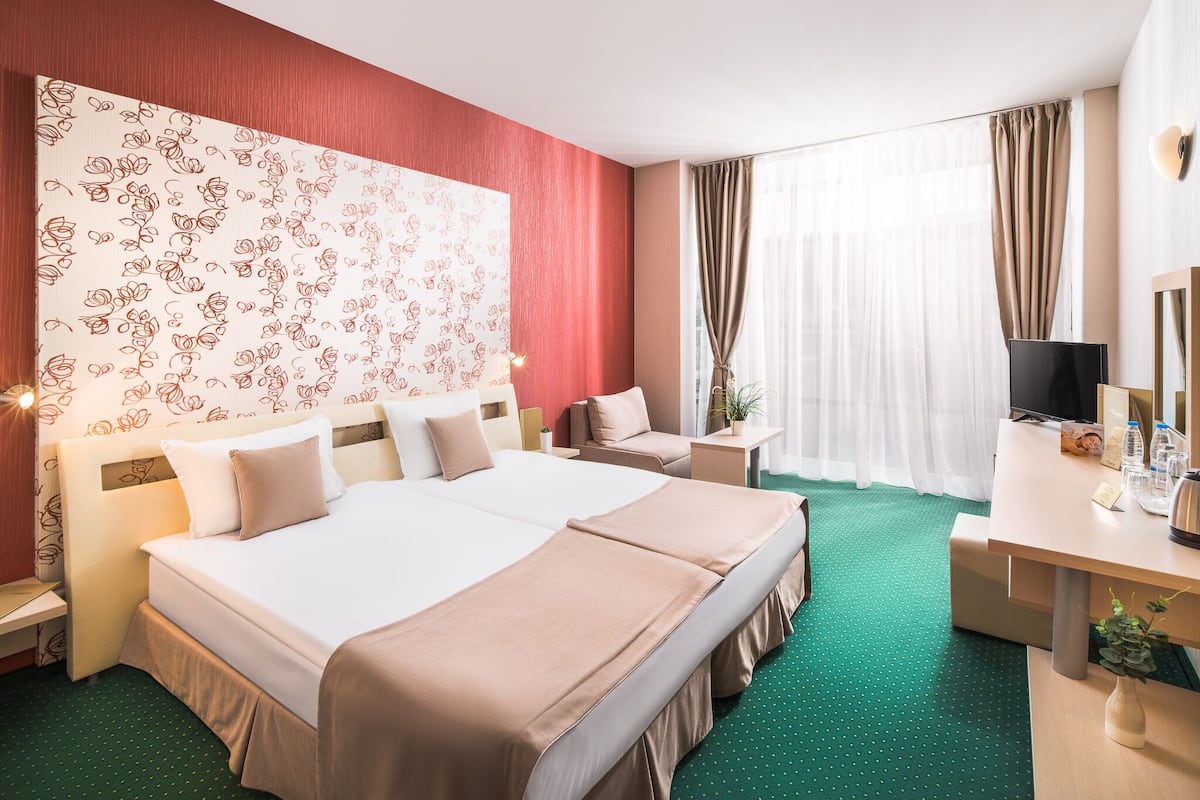 Quarto de hotel com uma cama grande, uma escrivaninha, uma cadeira e uma televisão.