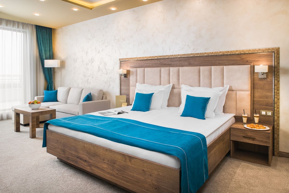 Quarto de hotel com cama grande, sofá, mesa de cabeceira e abajur.