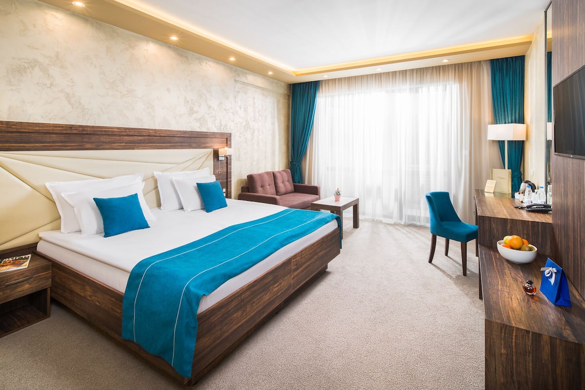 Quarto de hotel com uma cama grande, uma escrivaninha, uma cadeira, uma televisão e um balcão de recepção.