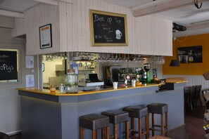 Uma área de bar com banquetas, um menu em lousa e um balcão com diversos itens.