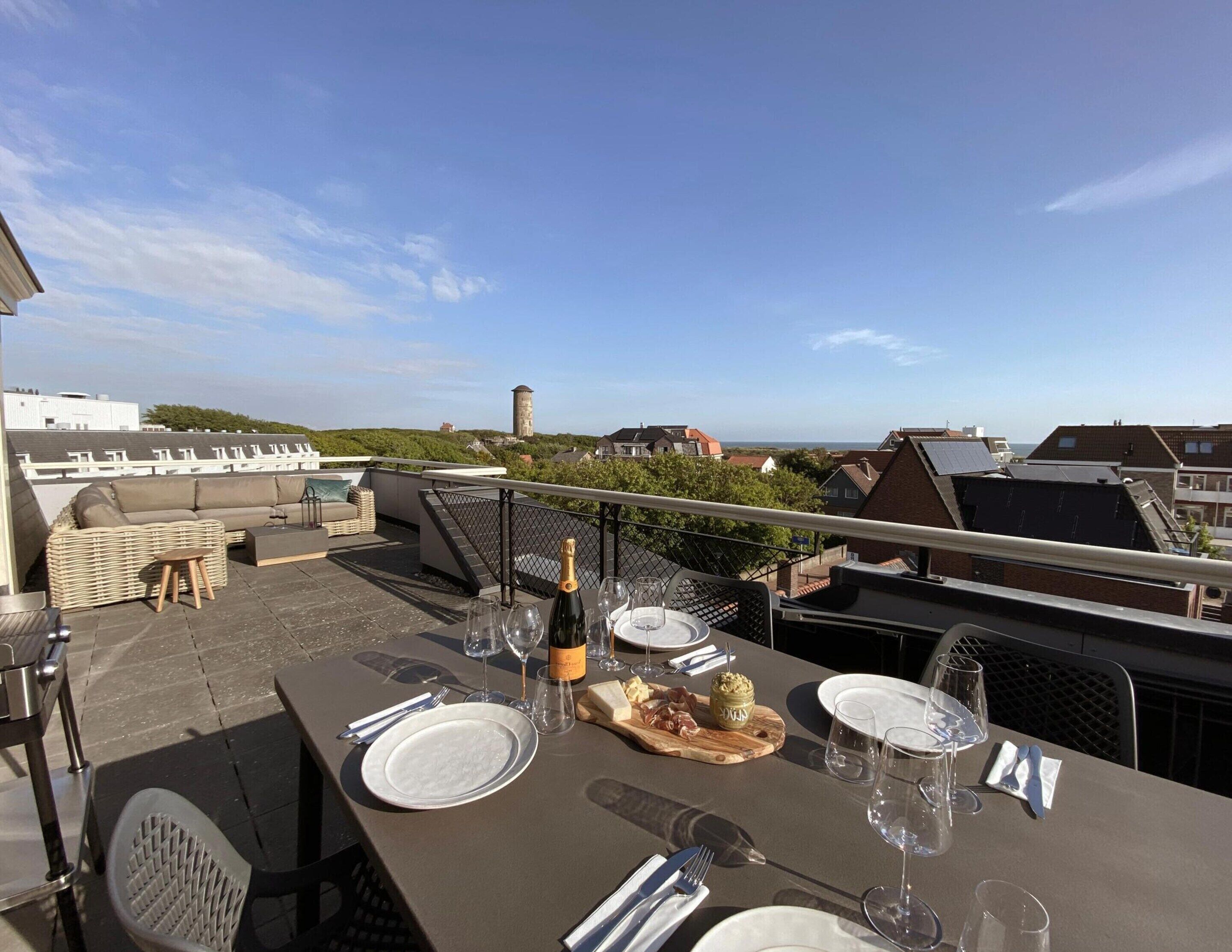 Terraço no telhado com mesa posta para refeições, vista para a paisagem urbana e o mar.