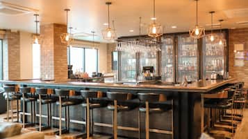 Uma área de bar moderna com ilha central, vários bancos altos, iluminação pendente e um painel de parede de tijolos.