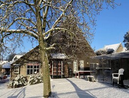 Um edifício de madeira com telhado inclinado, área de estar coberta ao ar livre e paisagem coberta de neve.